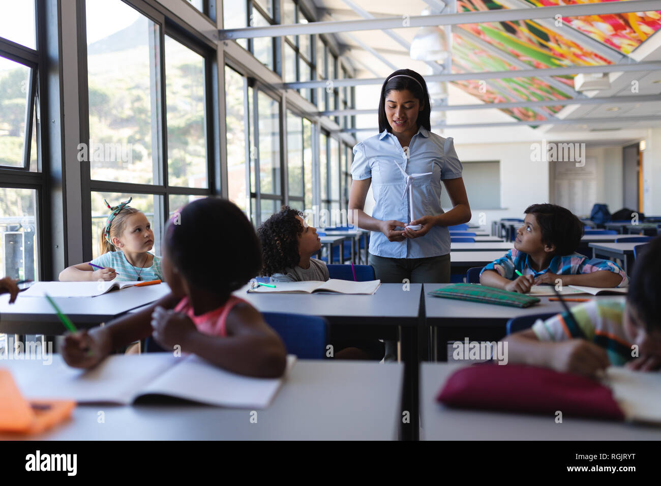 Front view of female teacher teaching student at desk in classroom of ...