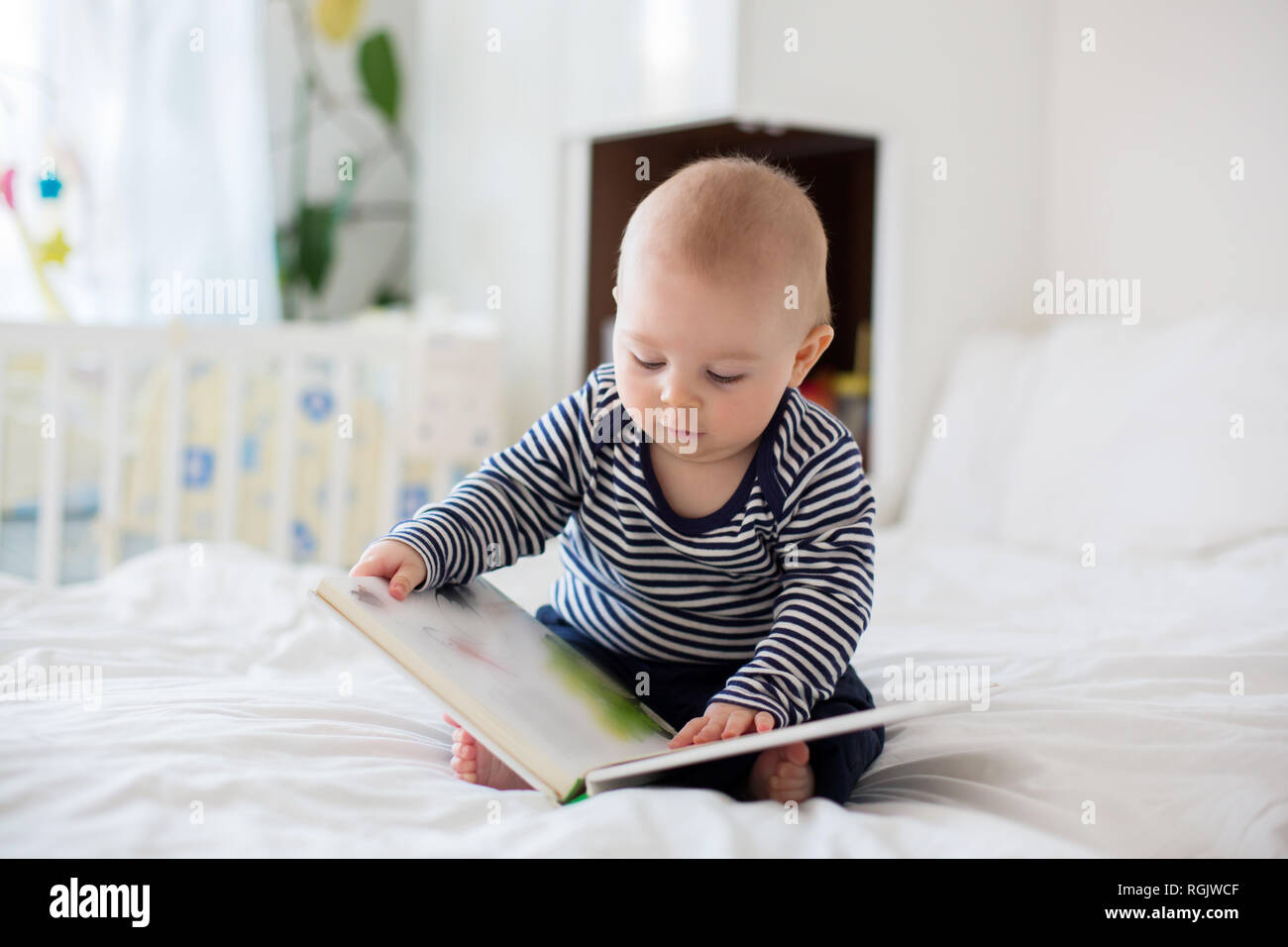 Portrait of a cute smiling infant baby boy reading a book. Happy ...