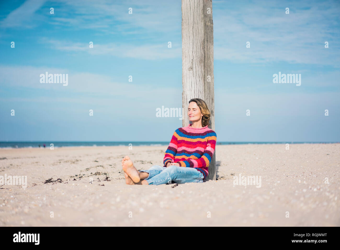 Mature woman relaxing on the beach, leaning on a pole Stock Photo - Alamy