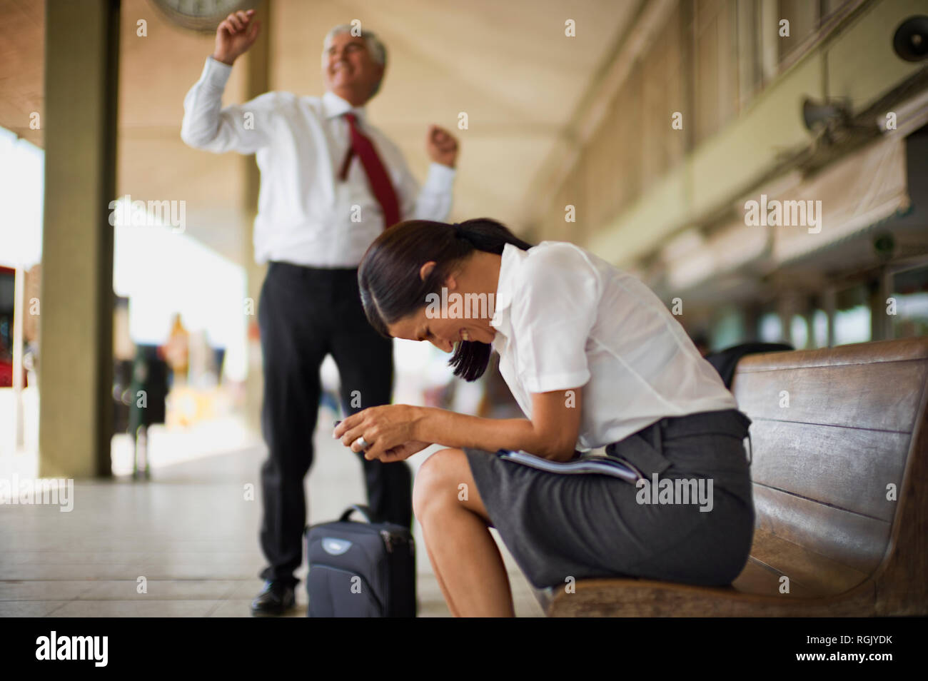 Businesswoman sitting on bench at a transport station laughs with ...