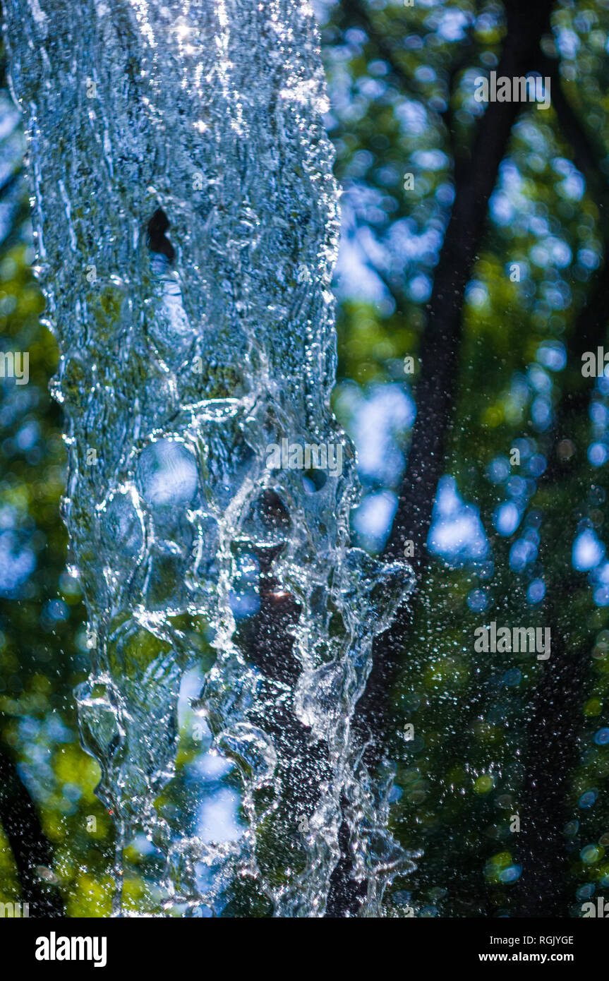 transparent falling water vertical flows against a blue sky and green ...
