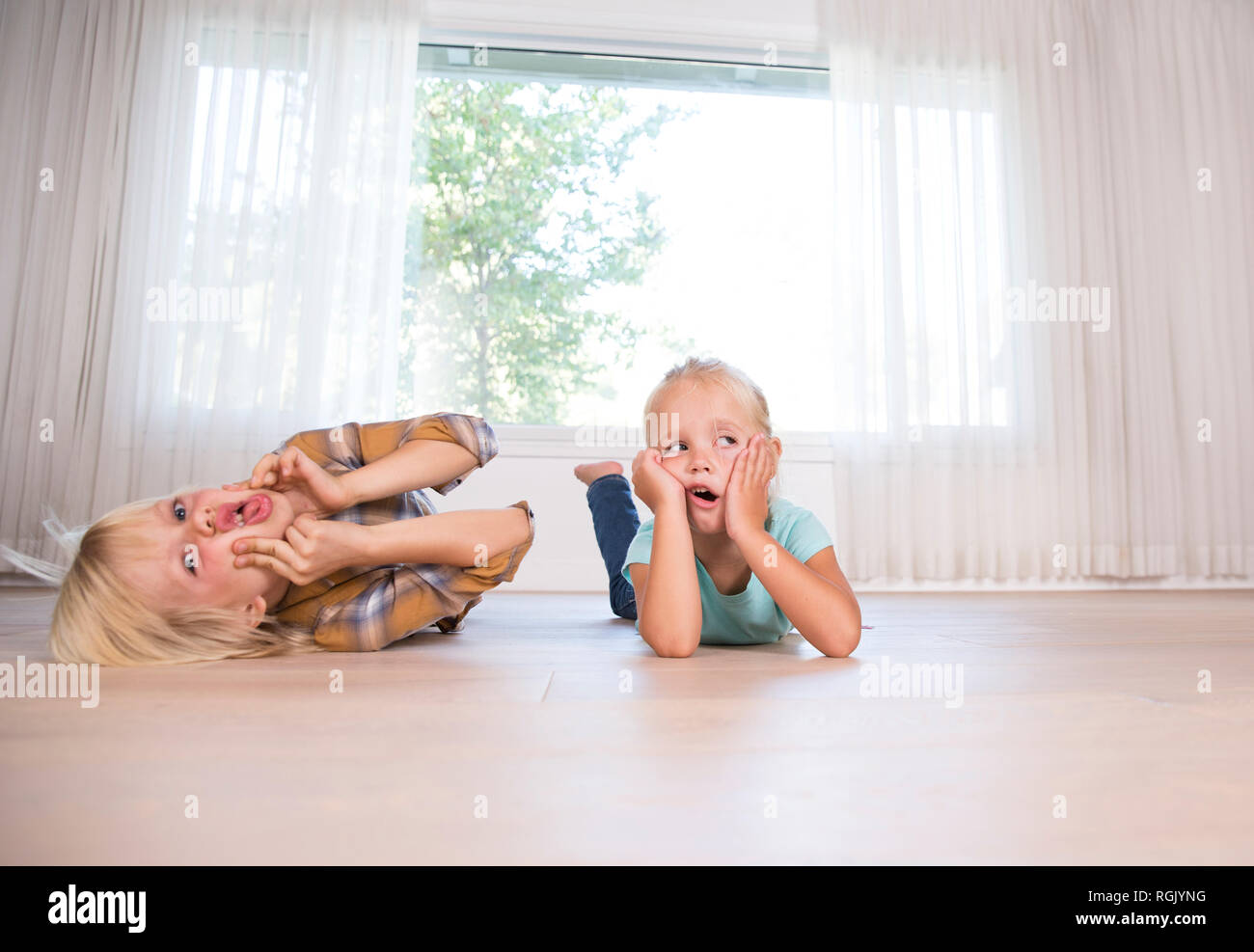 Brother and sister lying on the floor at home grimacing Stock Photo - Alamy