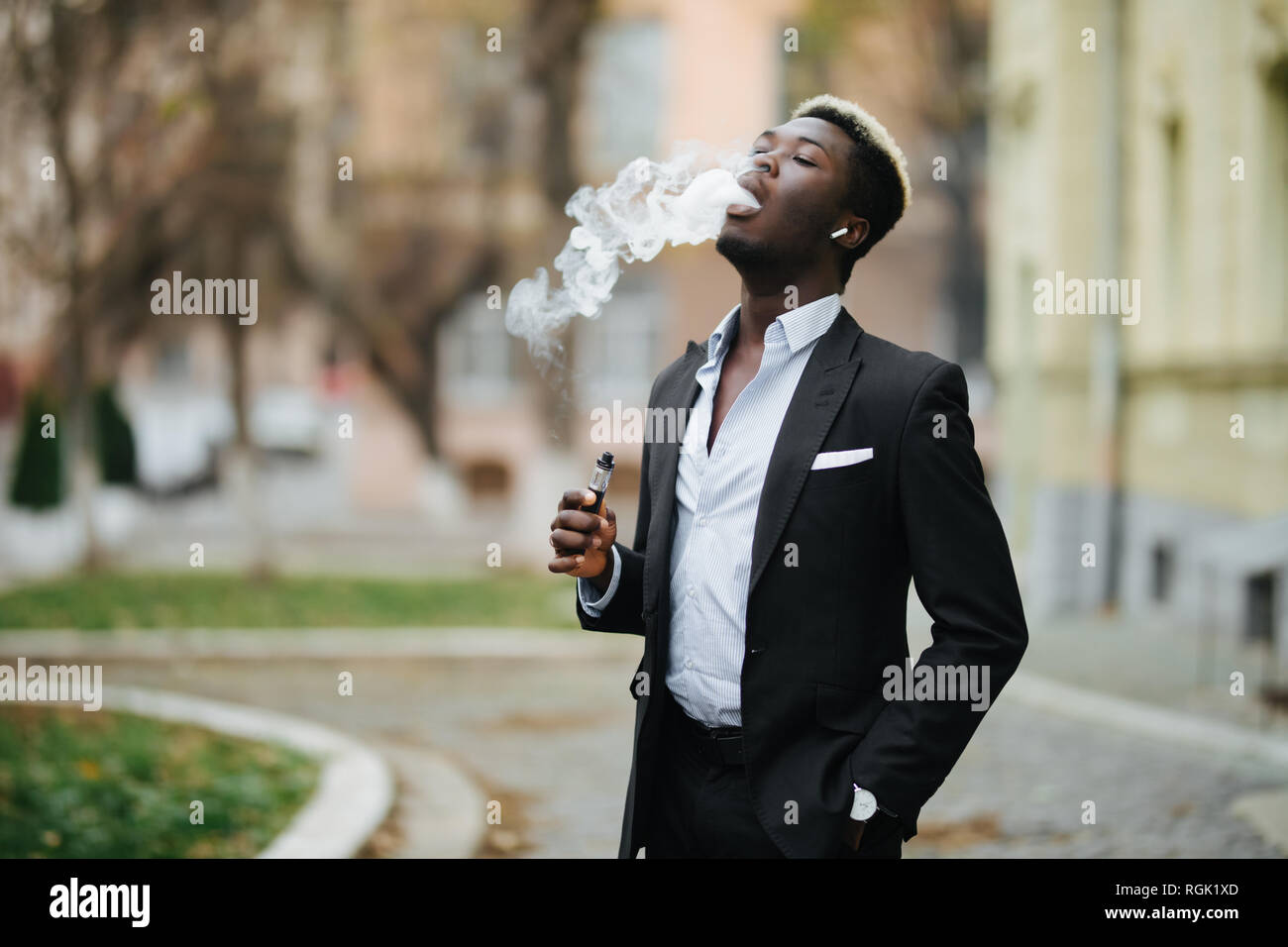 African man in a suit strolling on the streets of the city with vaping ...