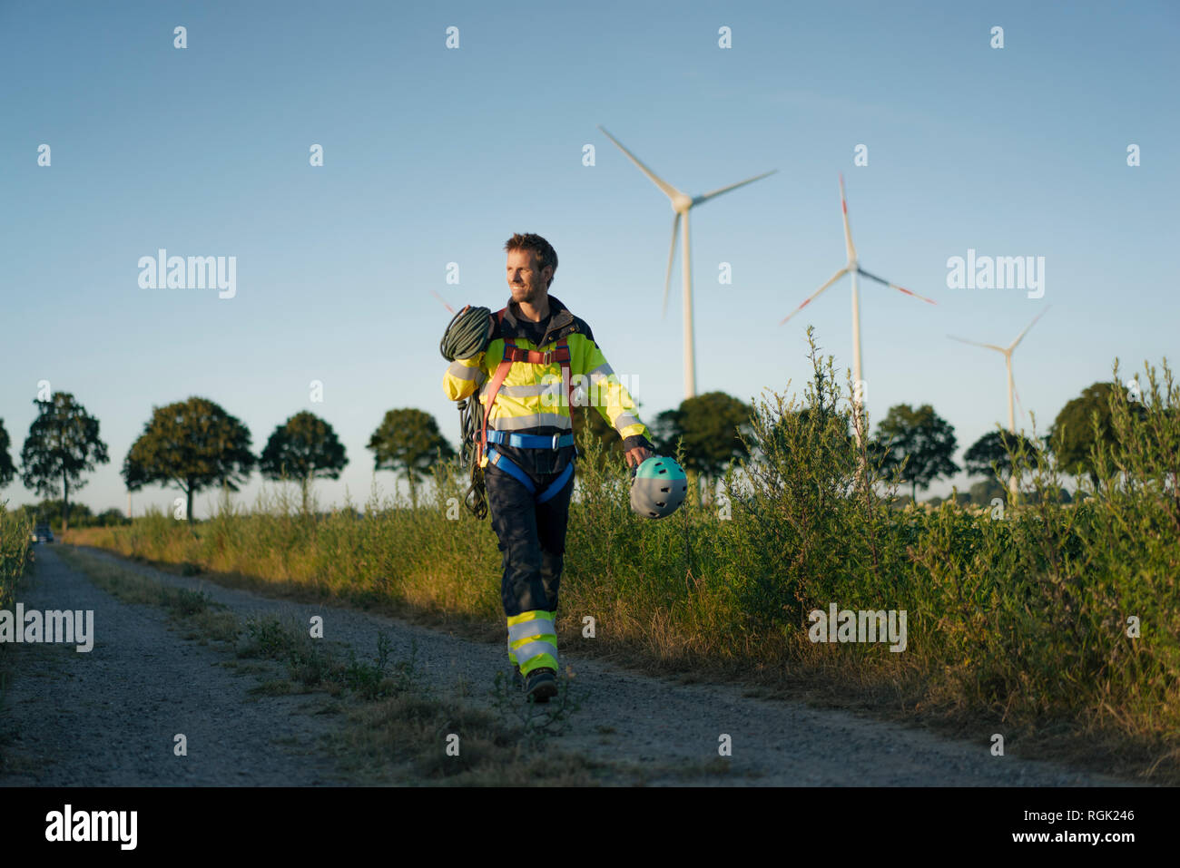 Technician walking on field path at a wind farm with climbing equipment ...