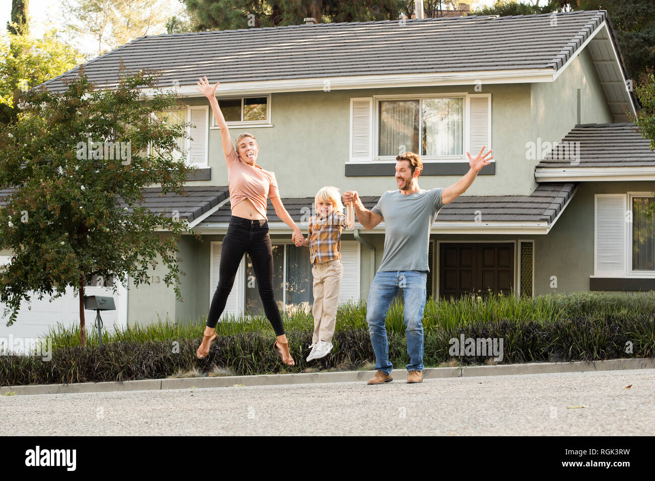 Happy family with son jumping in front of their home Stock Photo - Alamy