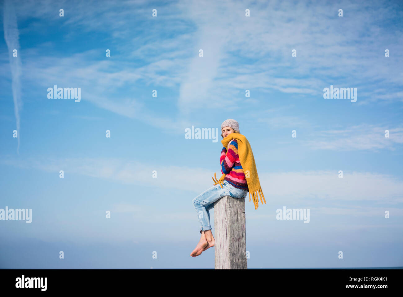 Mature woman sitting on a wood pole on the beach Stock Photo - Alamy