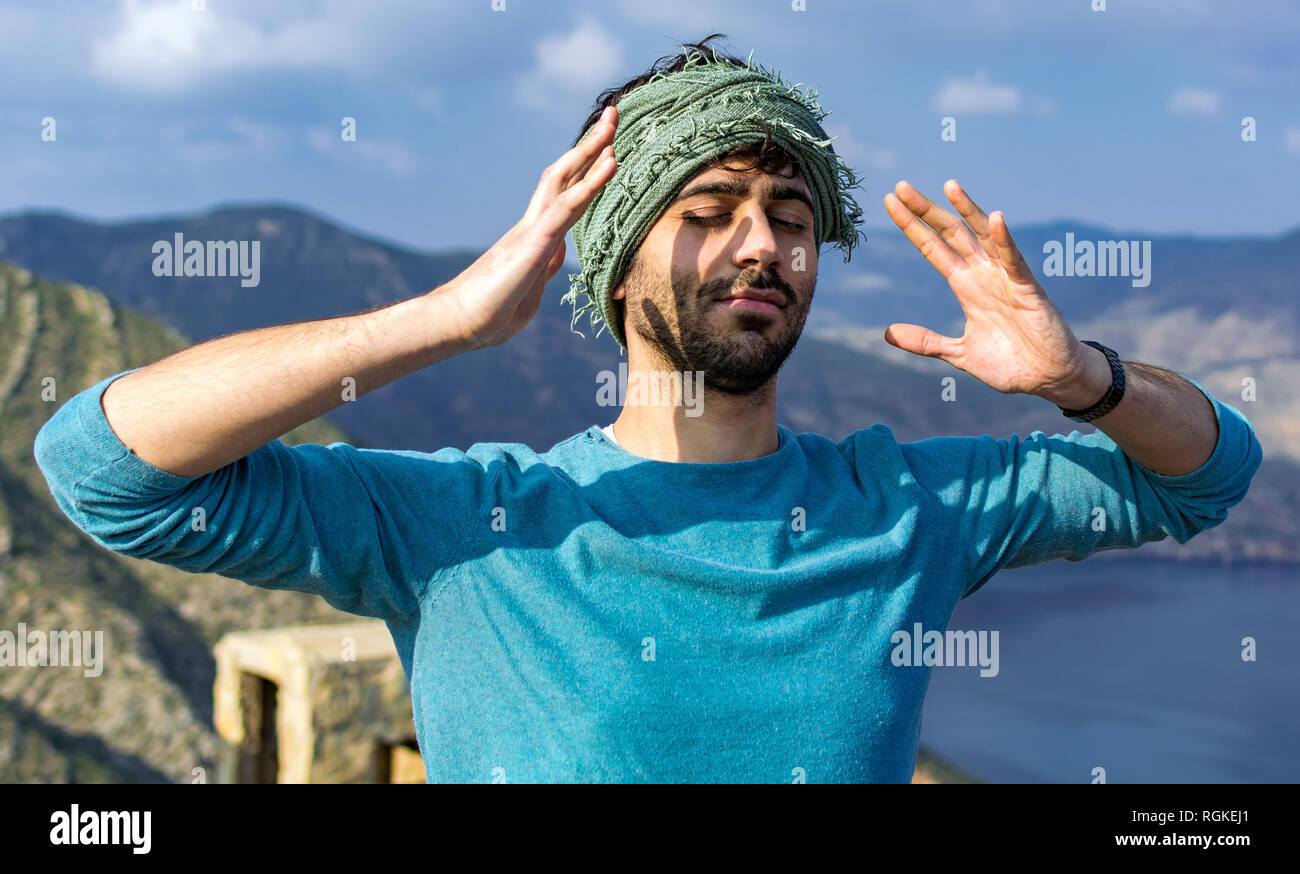 Young Indian man on hill top edge cliff rock performing yoga at a ...