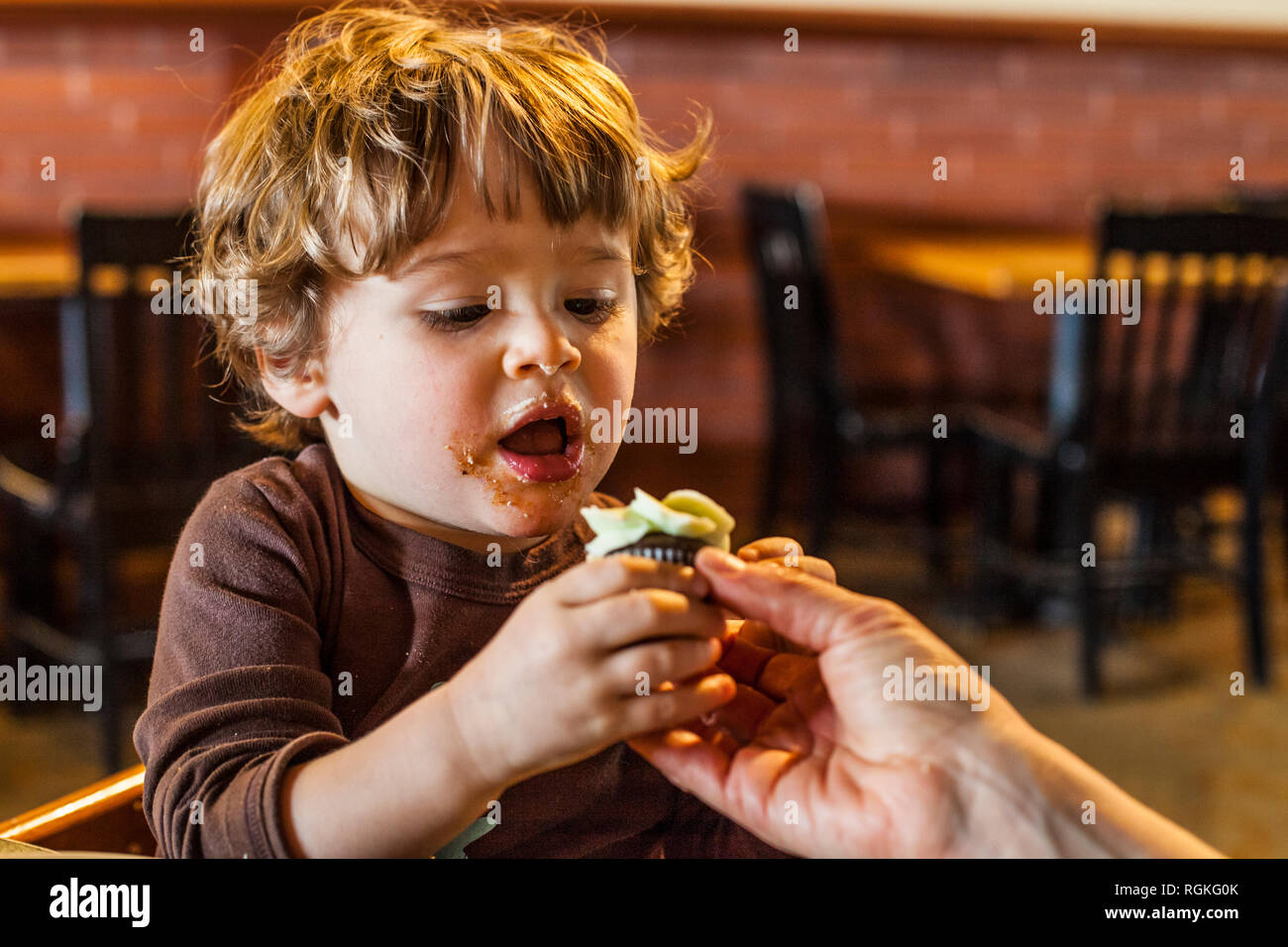 A toddler with a messy face taking a cupcake from his mothers hands ...