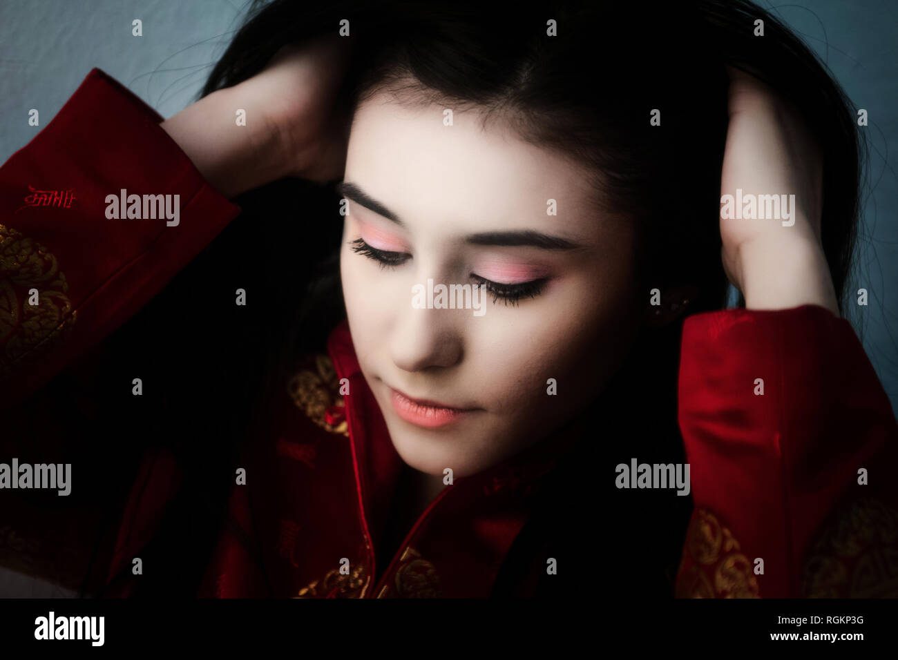 Image of a pretty young girl looking down in Asian inspired red top ...