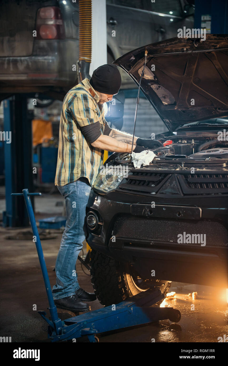 Car service. Brutal mechanic man standing by the car with open hood and ...