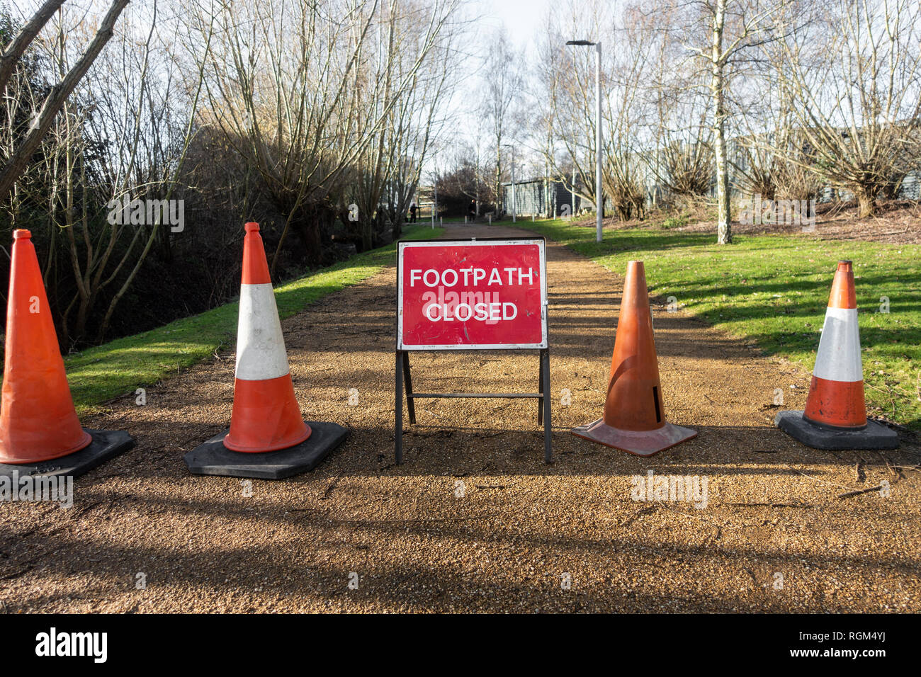 A footpath through parkland is closed and a sign and orange cones block ...