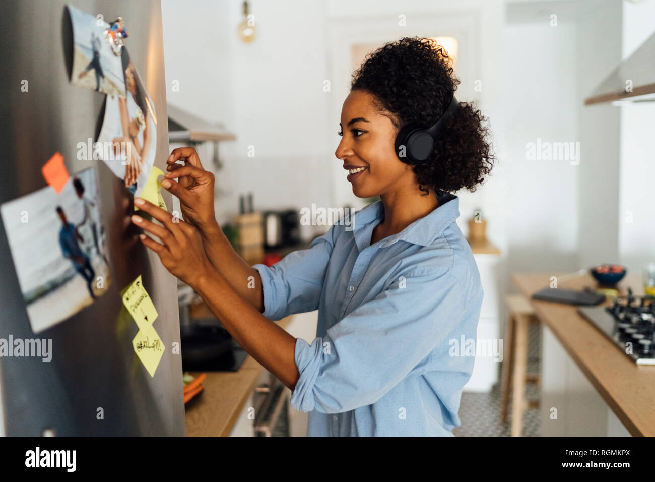Woman in her kitchen in the morning, posting sticky notes on the fridge ...