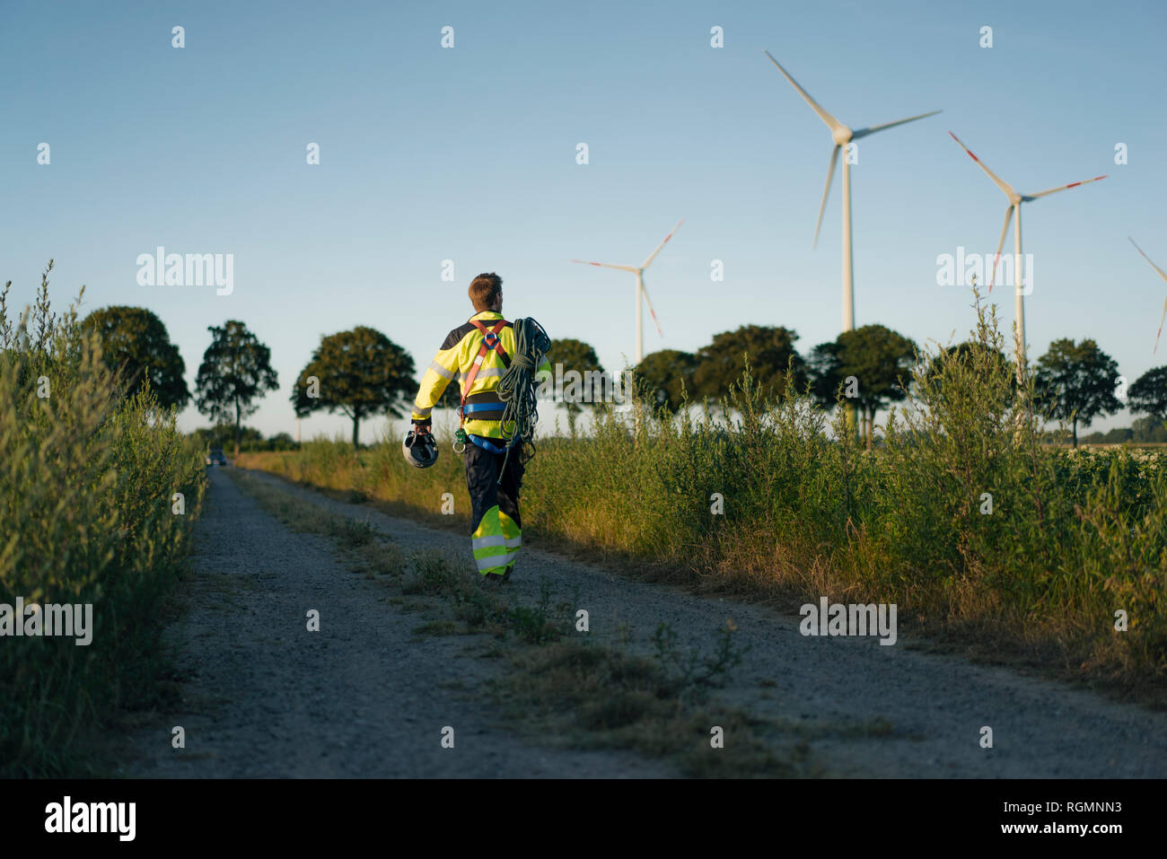 Technician walking on field path at a wind farm with climbing equipment ...