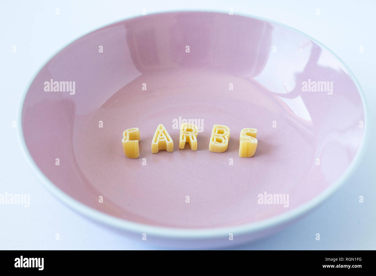 The word "carbs" composed with real pasta letters in a pink dish Stock ...