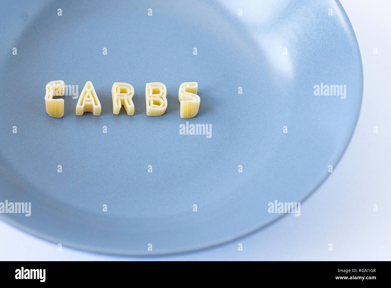 The word "carbs" composed with real pasta letters in a blue dish Stock ...