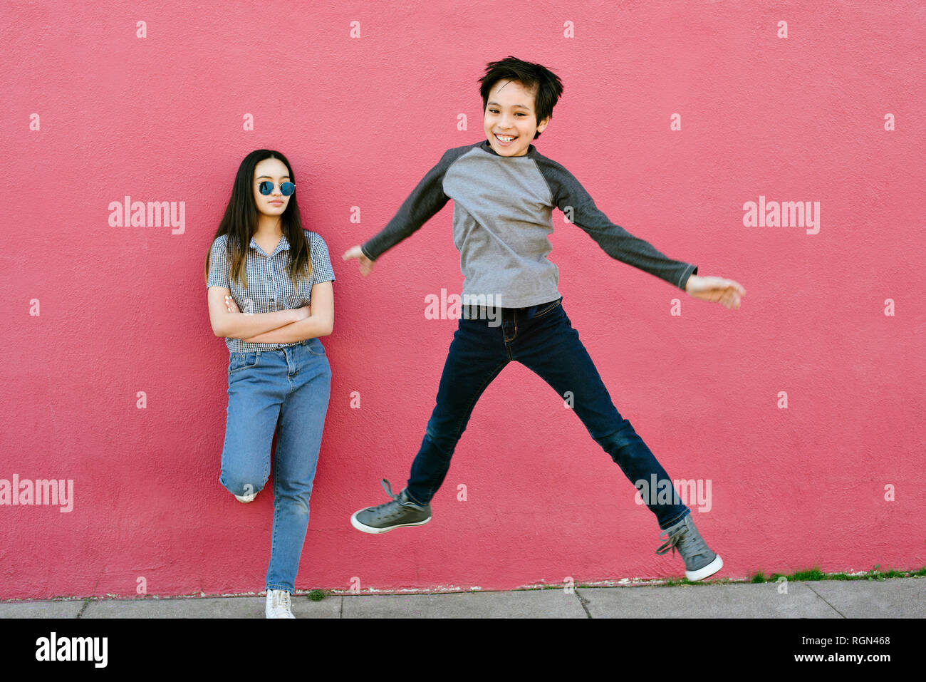A teen sister looks onto her younger brother as he leaps into the air ...