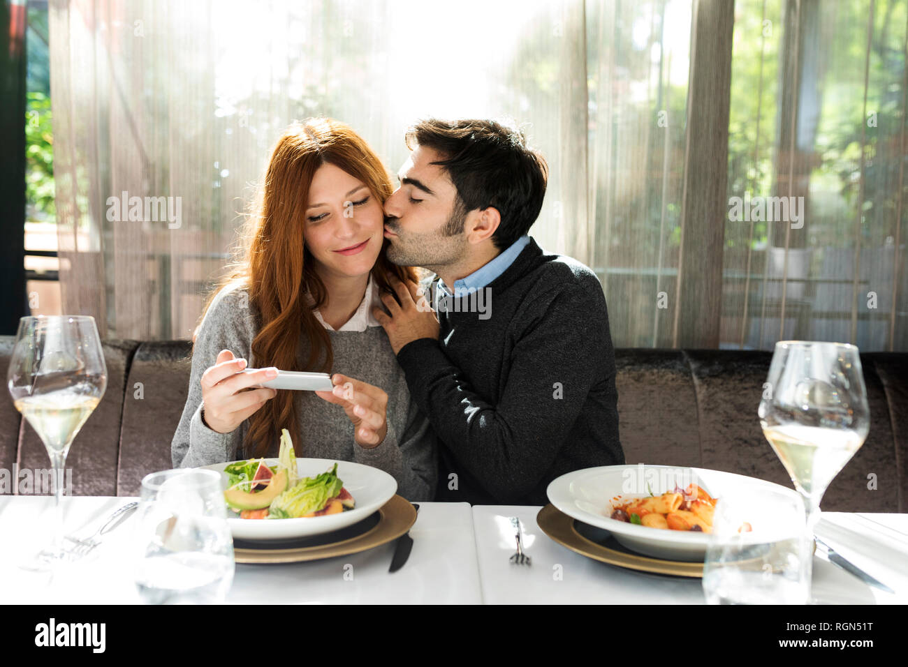Man kissing woman taking a cell phone picture in a restaurant Stock ...