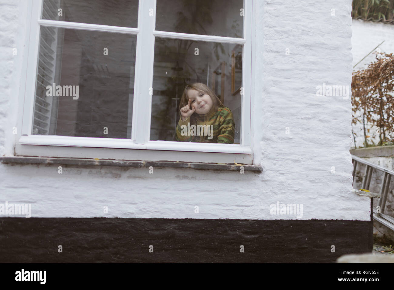 Smiling little girl looking out of window Stock Photo - Alamy