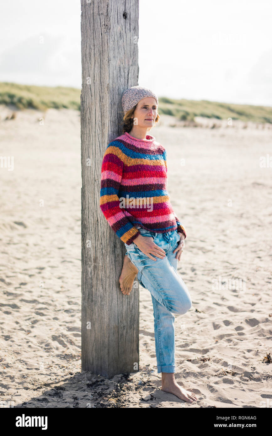 Mature woman relaxing on the beach, leaning on a pole Stock Photo - Alamy