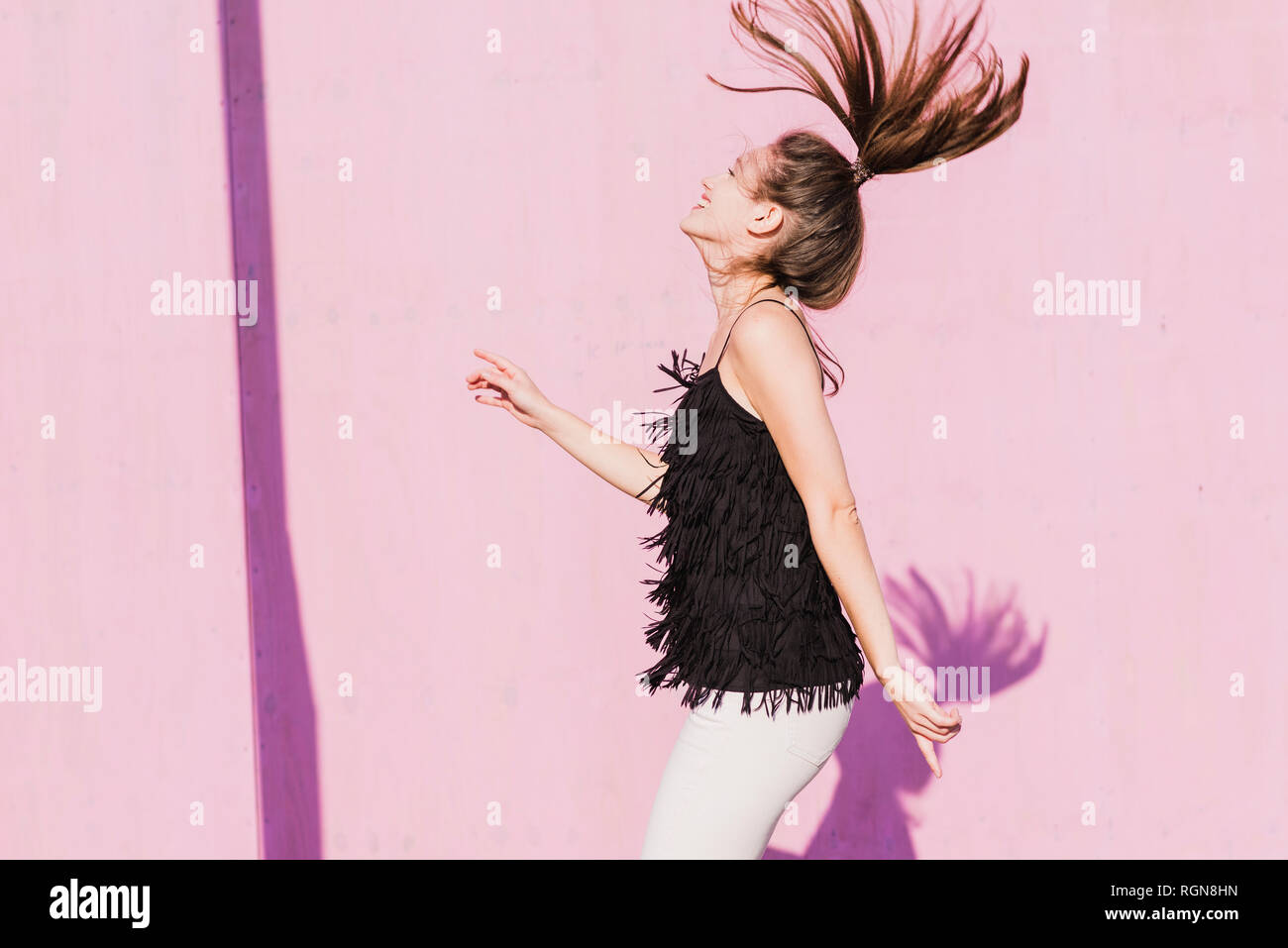 Happy young woman moving in front of pink wall Stock Photo - Alamy
