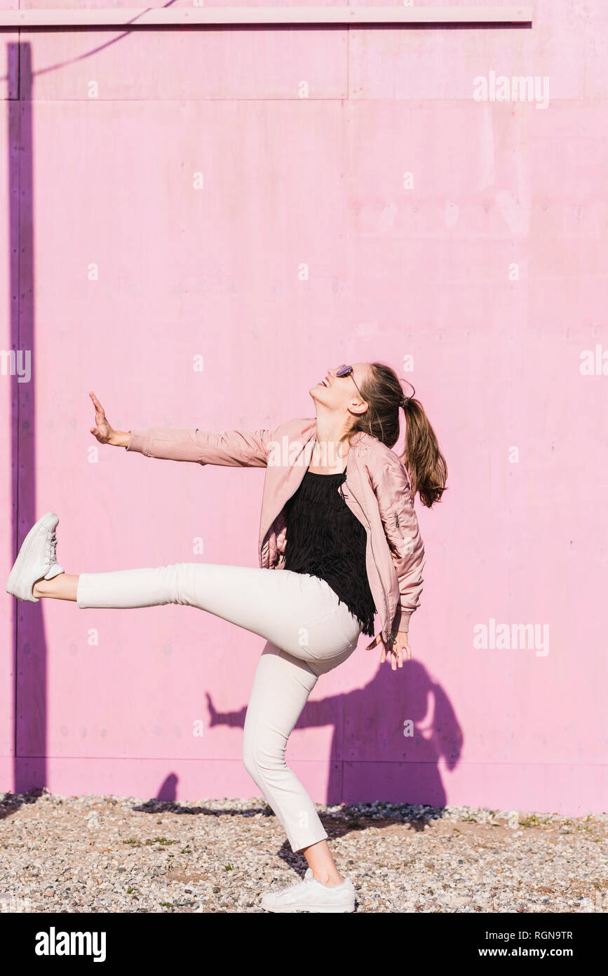 Happy young woman moving in front of pink wall Stock Photo - Alamy