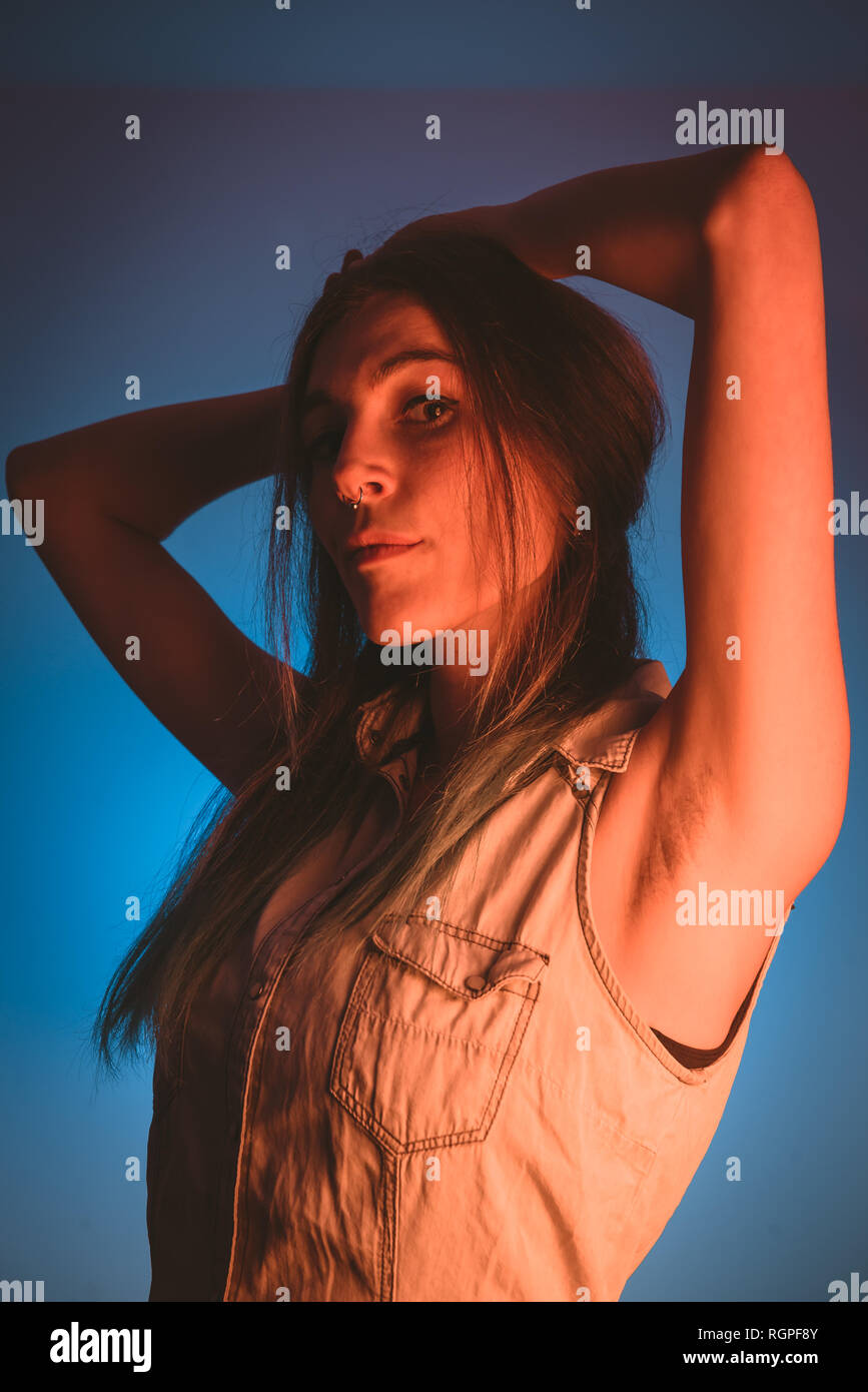 Charming young lady with piercing with arms up in the head looking at ...