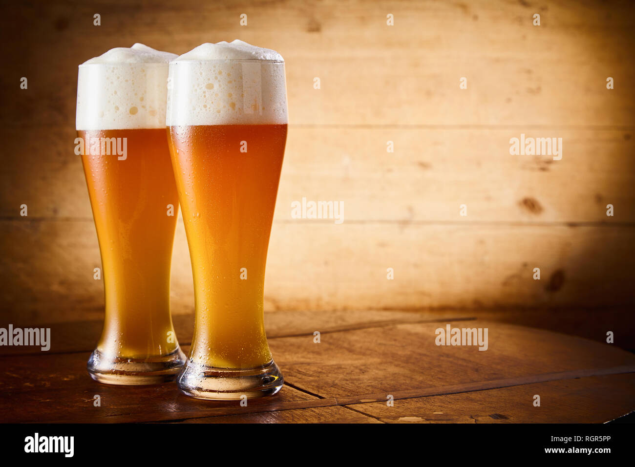 Two ice cold glasses of frothy larger or wheat draft beer on a rustic ...