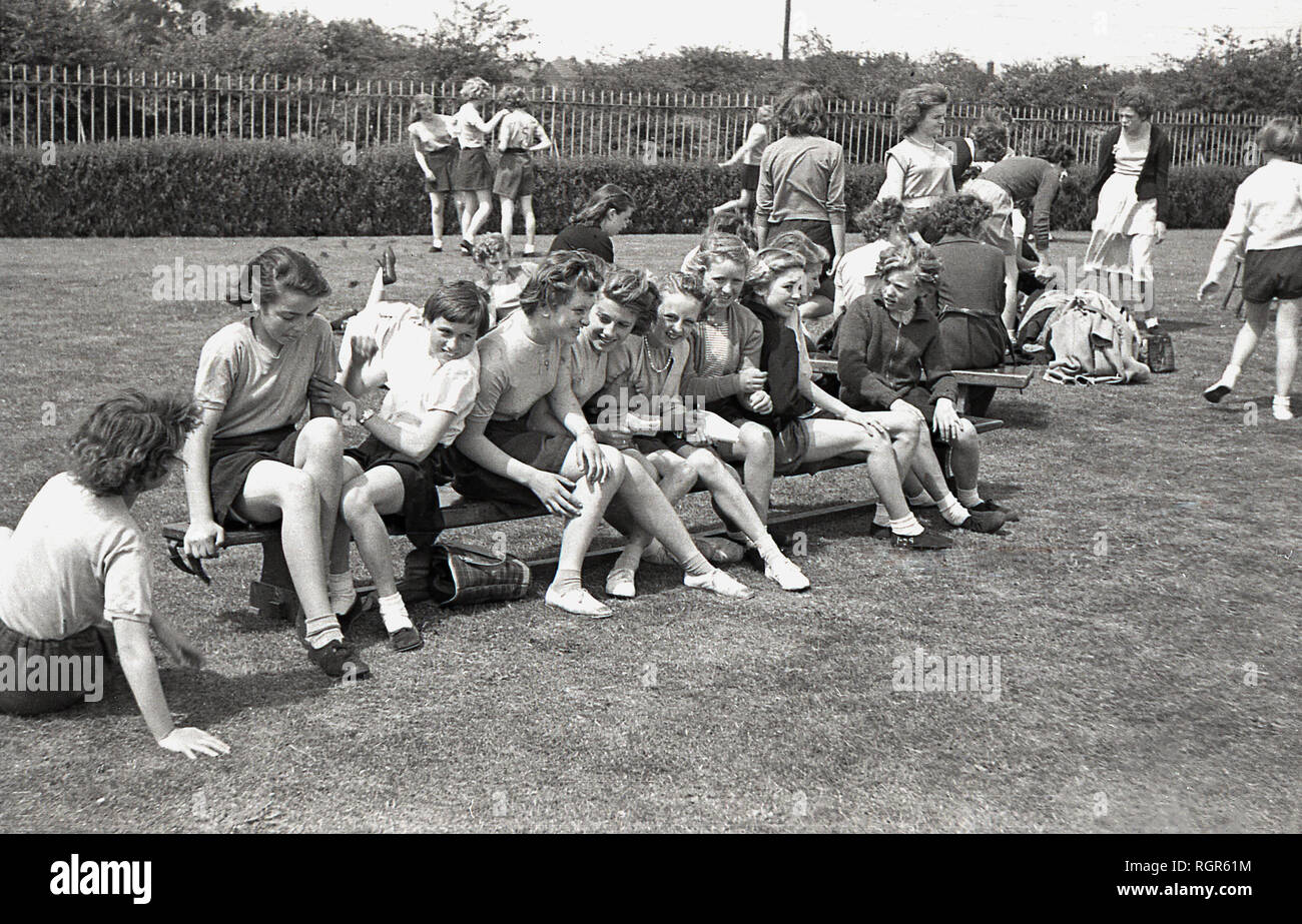 1950s, girls having fun chatting with each other sitting on a bench ...