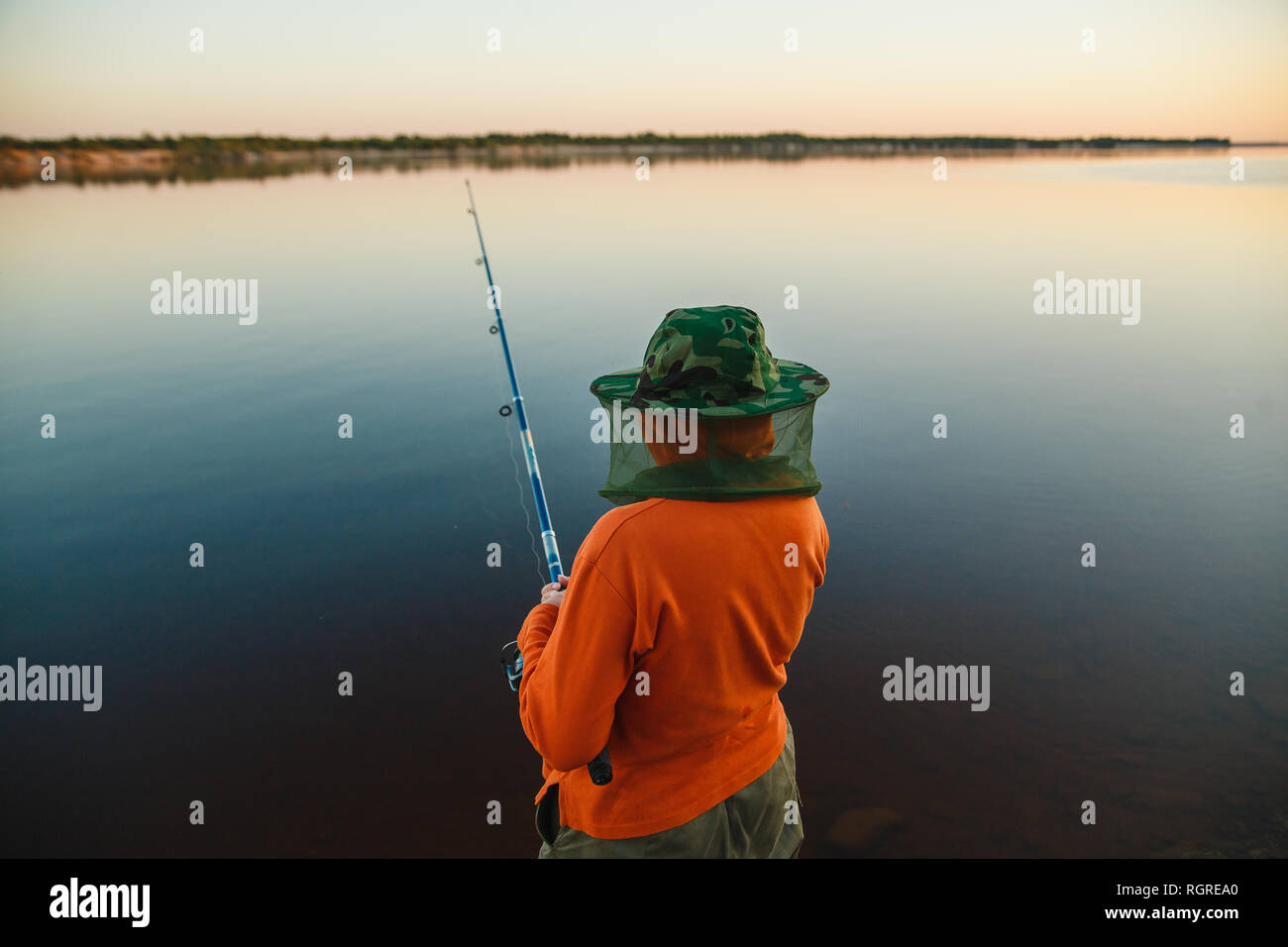 Back view of young woman in mosquito net fishing with fishing rod or ...