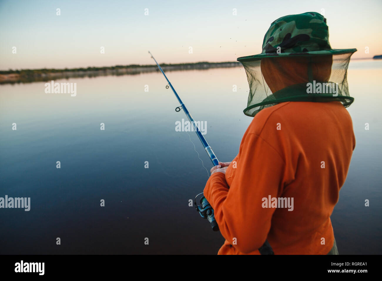 Back view of young woman in mosquito net fishing with fishing rod or ...