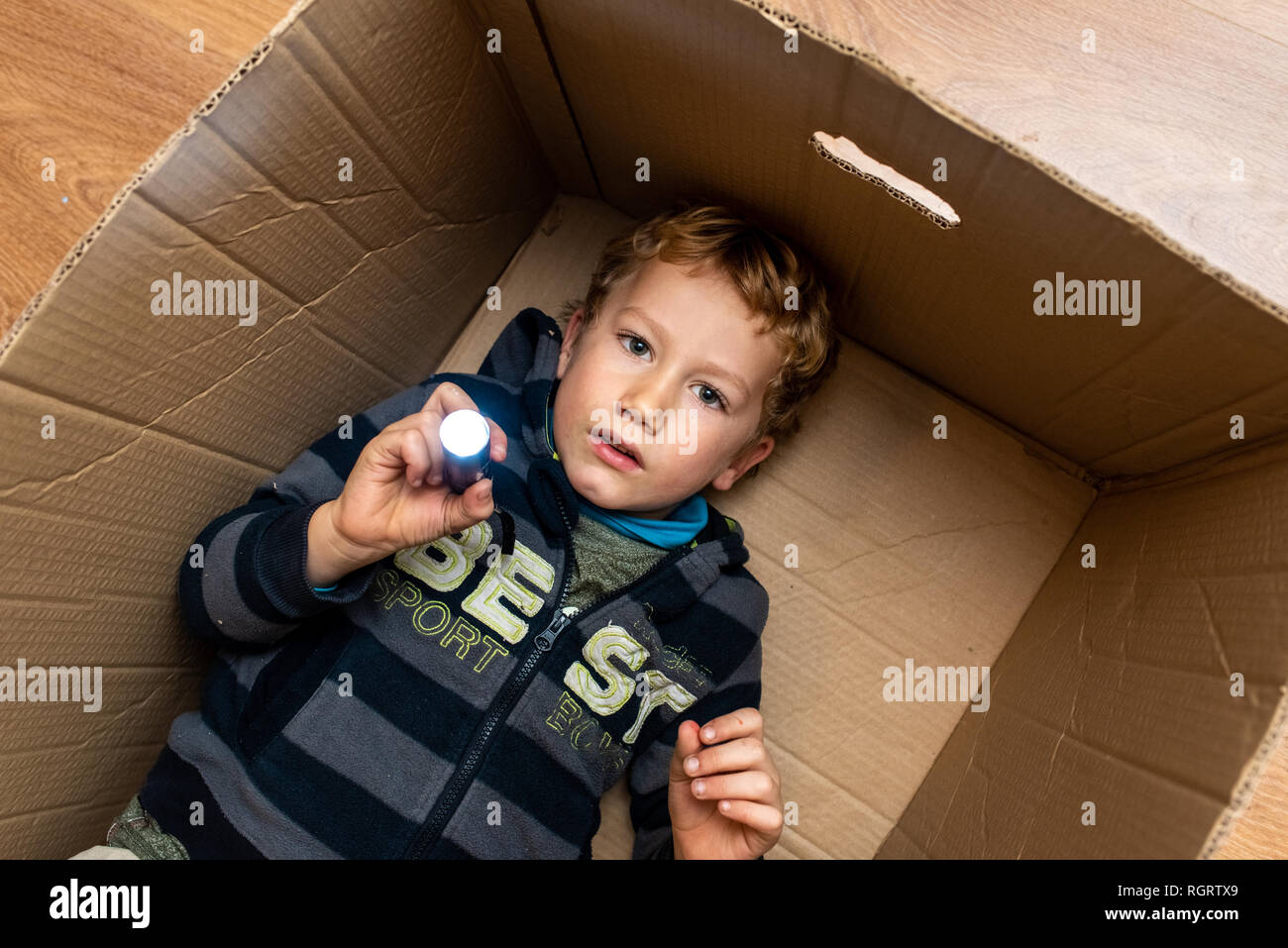 Child with flashlight inside cardboard box and expression of surprise ...