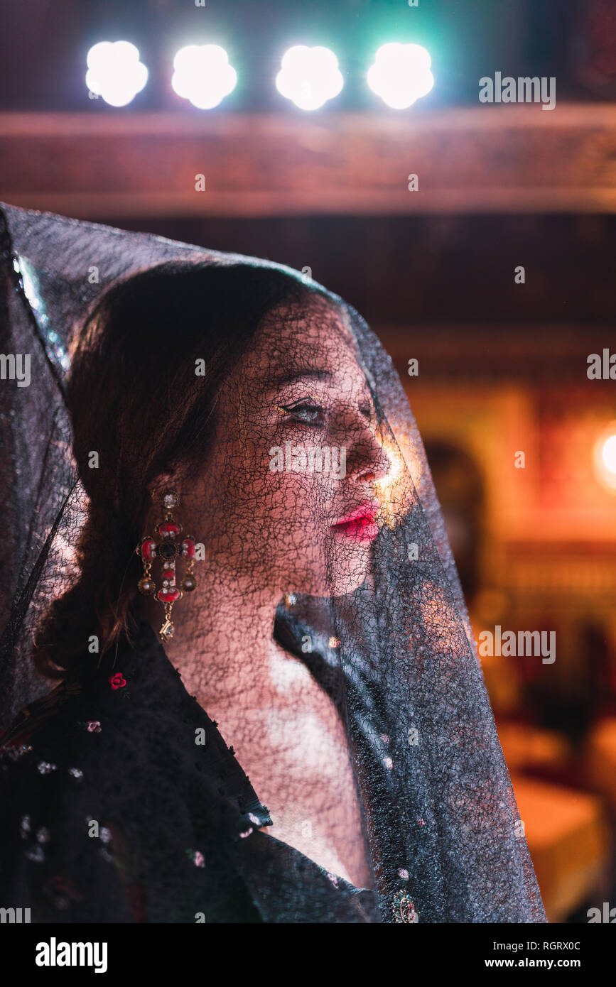 Side view of attractive lady in veil and dress on scene illuminated by ...