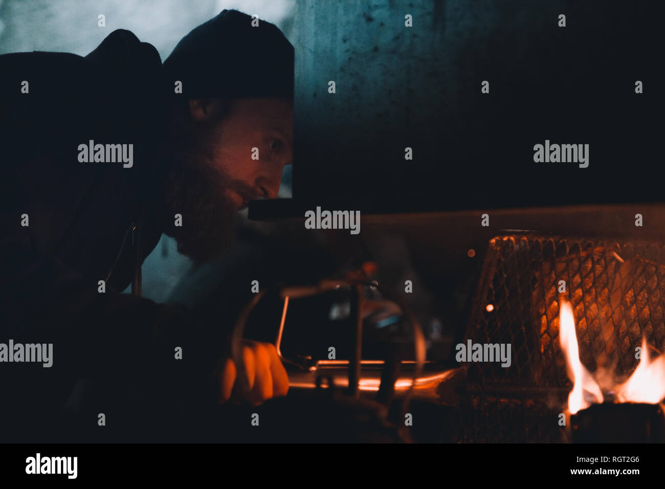 Side view of bearded guy looking inside flaming furnace in cold Arctic ...