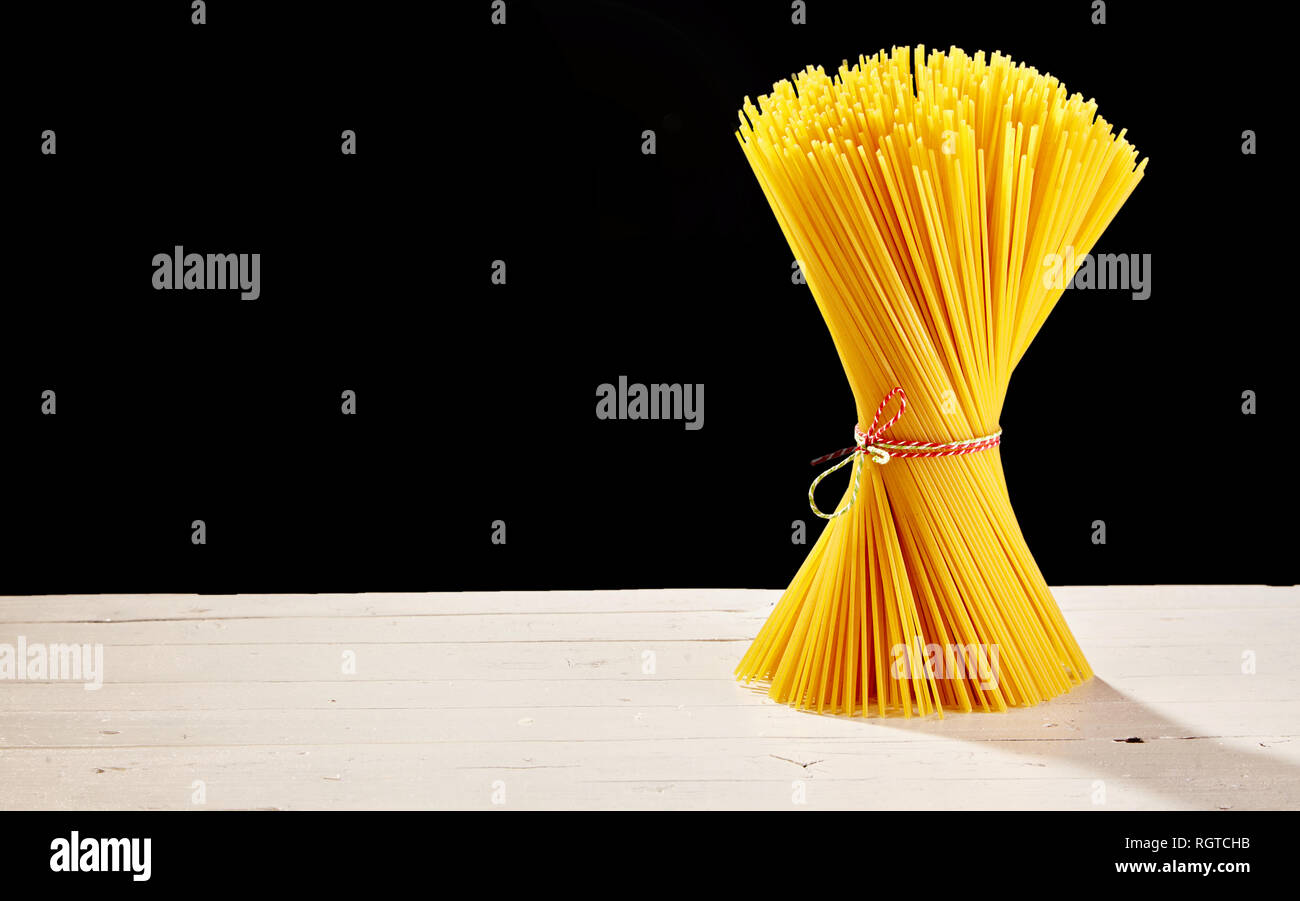 Golden spaghetti tied into a bunch with colourful string on a rustic ...