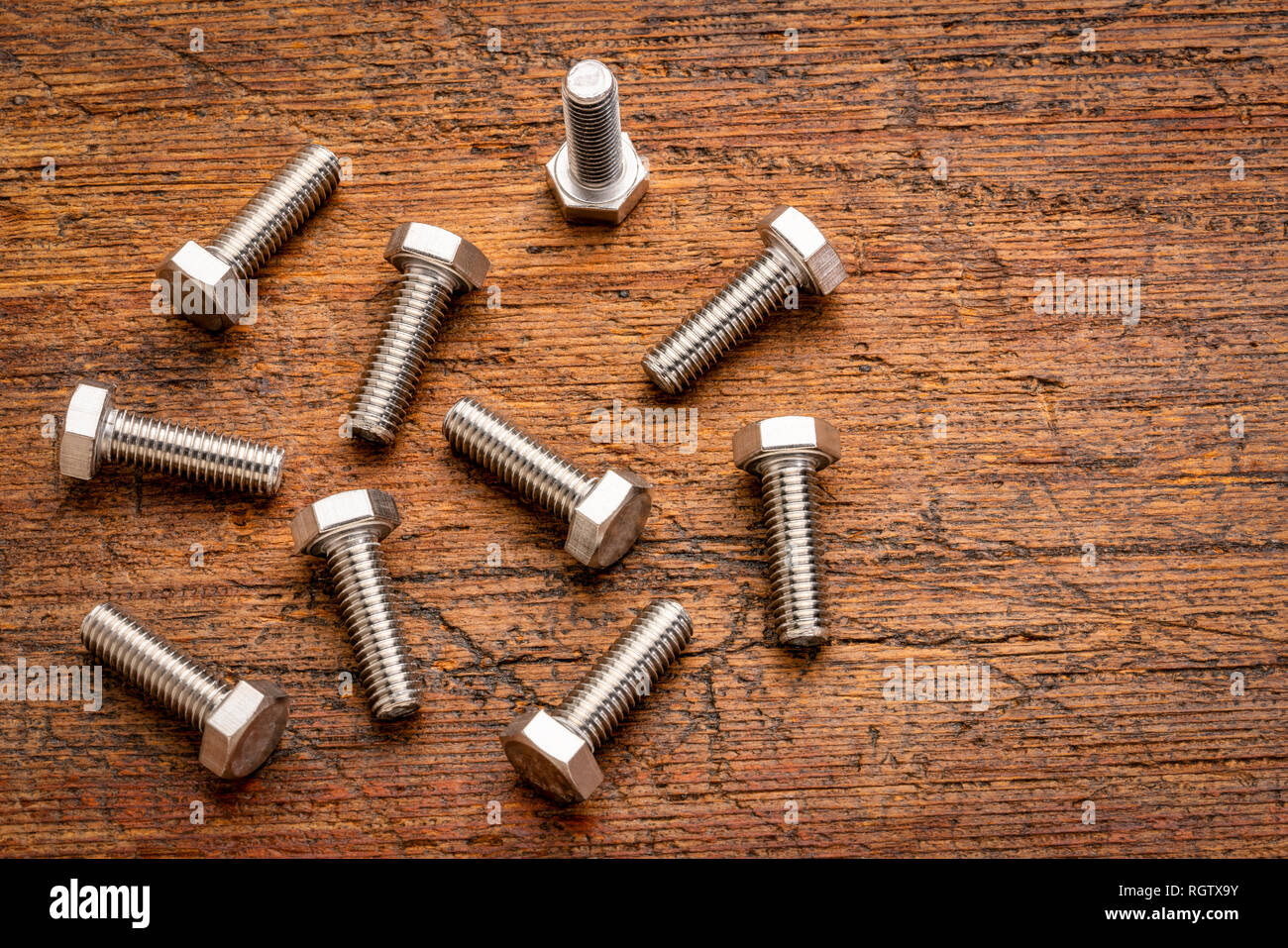 a set of ten hex stainless steel bolts against rustic wood with a copy ...