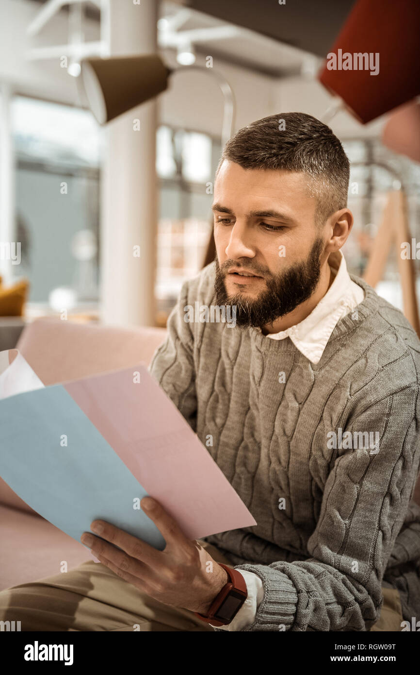 Concentrated good-looking man being busy with furniture shop brochure ...