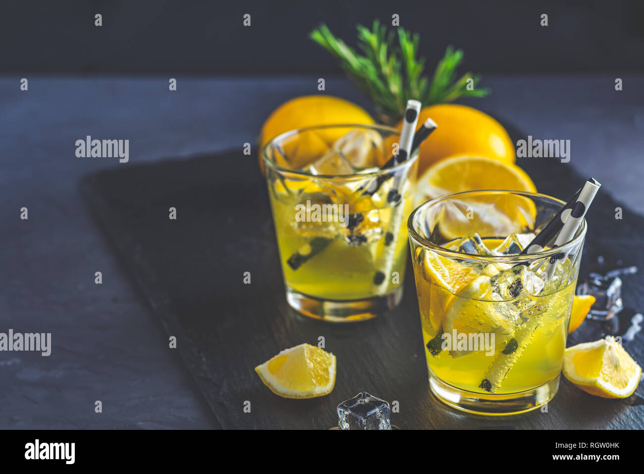 Lemon alcohol drink cocktail with ice, lemon and rosemary herb on black ...