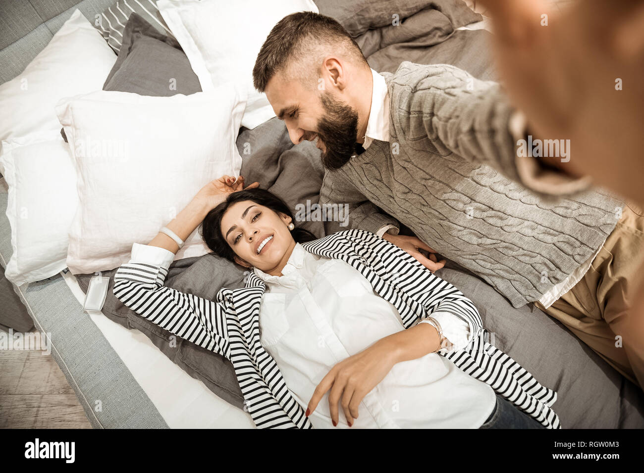 Appealing dark-haired woman relaxing on bed while her husband making ...