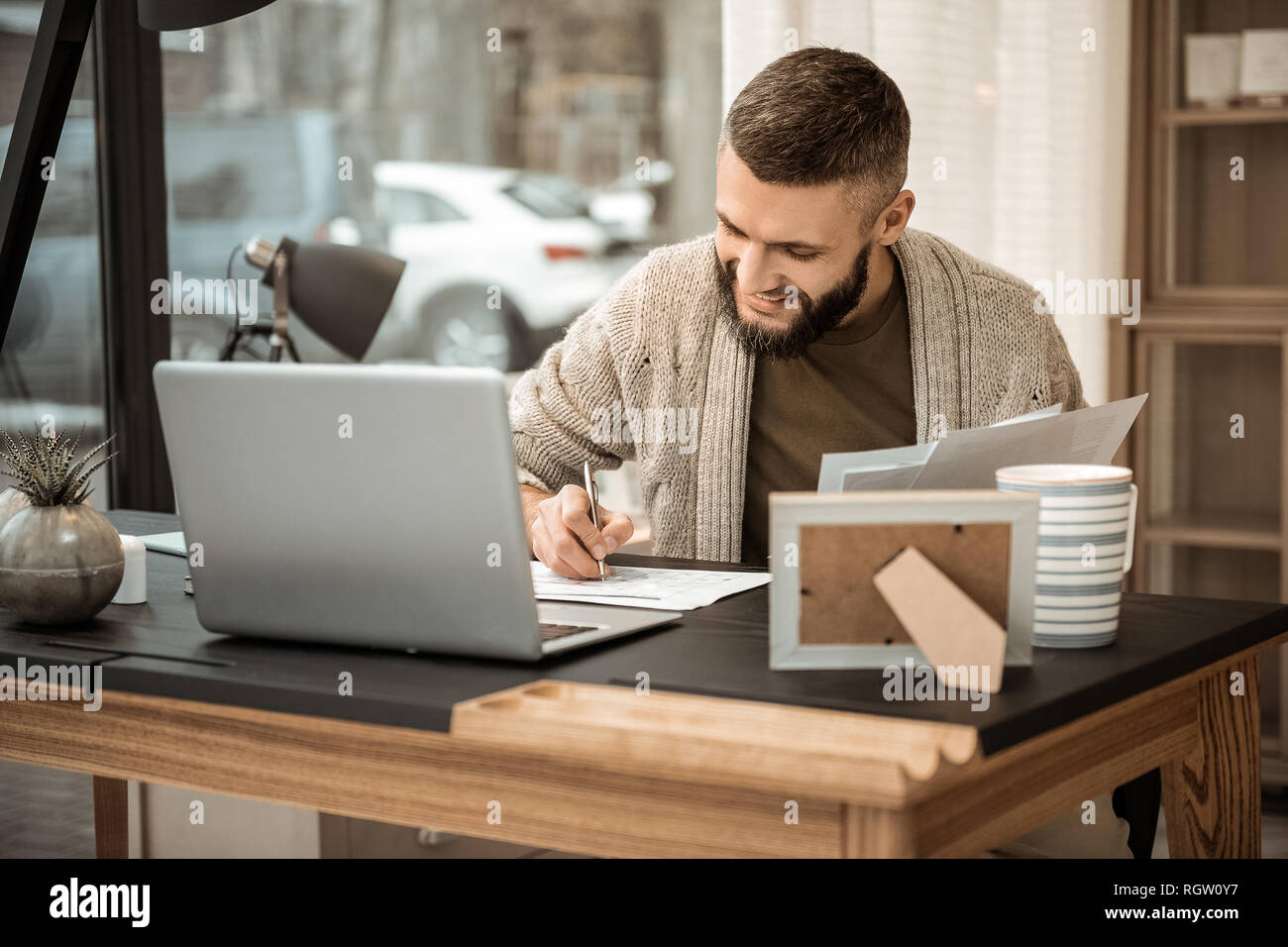 Smiling positive business man in grey cardigan writing down meeting ...