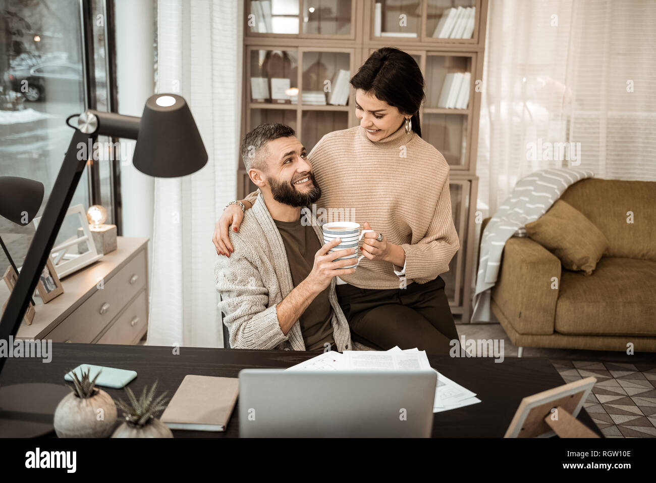 Joyful positive couple hugging each other and sharing hot tea Stock ...