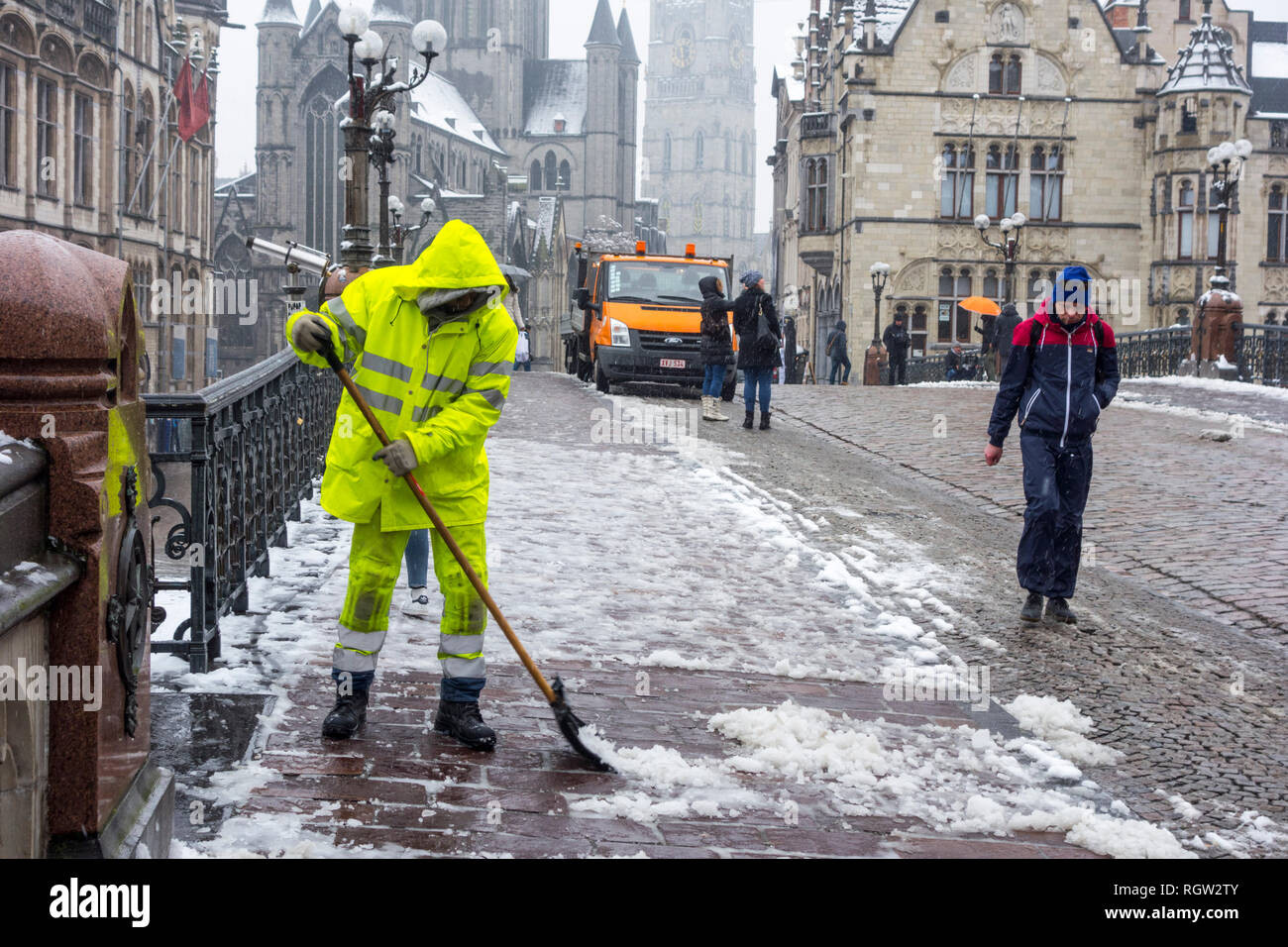 Pedestrians on slippery road and city worker cleaning pavement during ...
