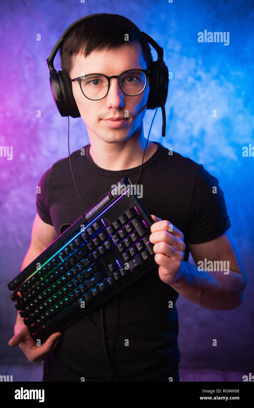 Computer nerd with keyboard over colorful pink and blue neon lit wall ...