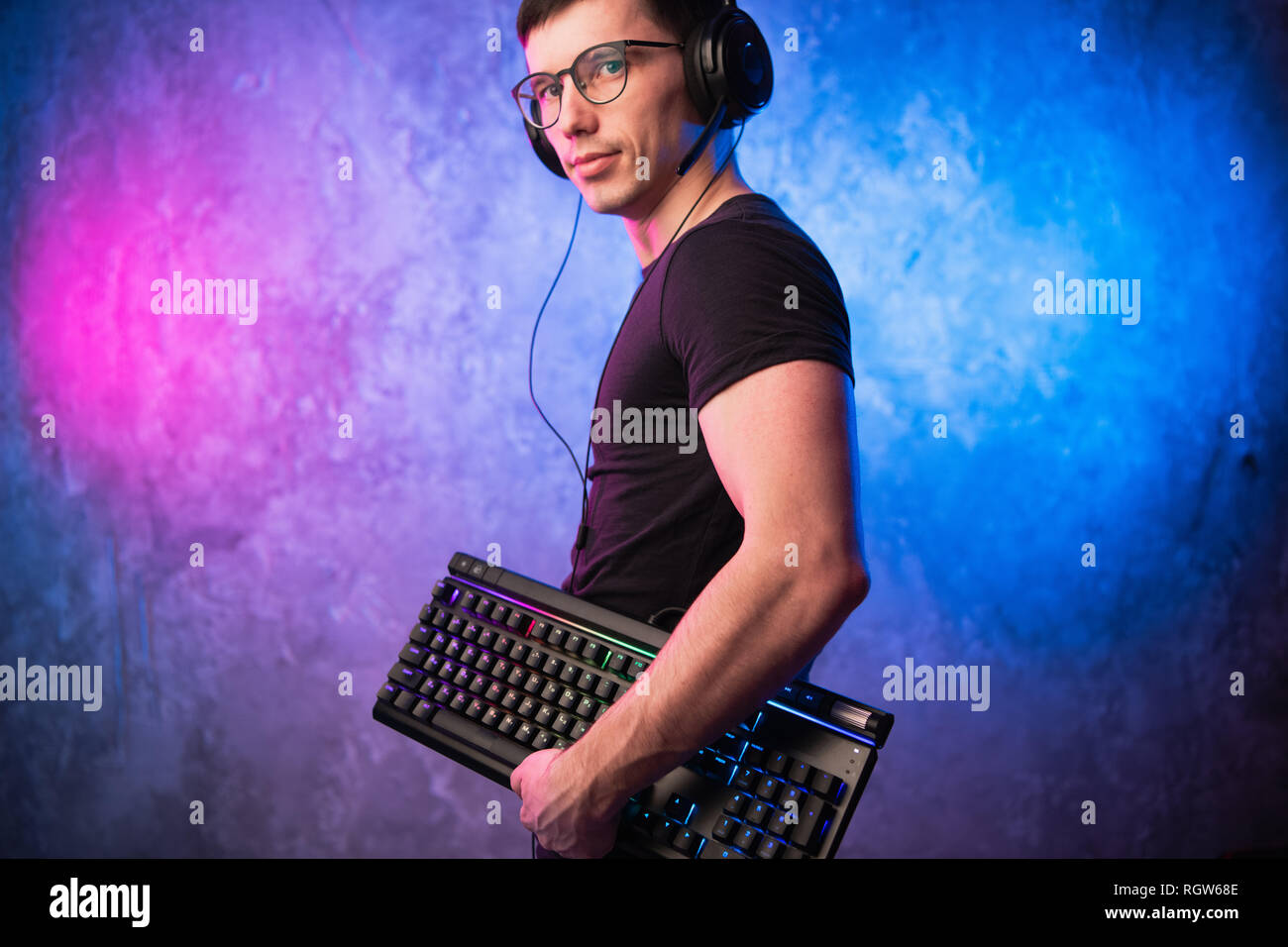Computer nerd with keyboard over colorful pink and blue neon lit wall ...