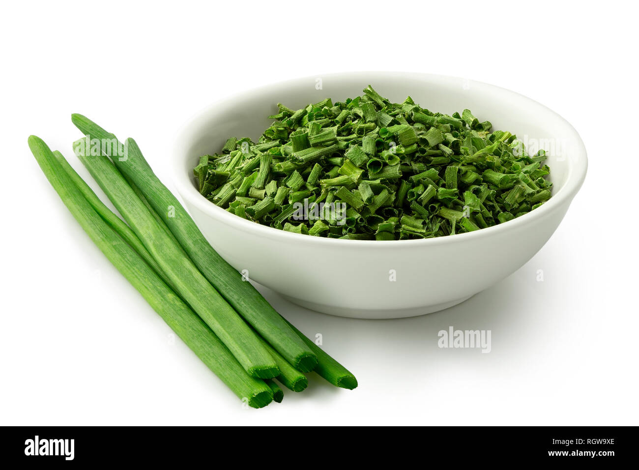 Dried chopped chives in white ceramic bowl next to a pile of whole ...