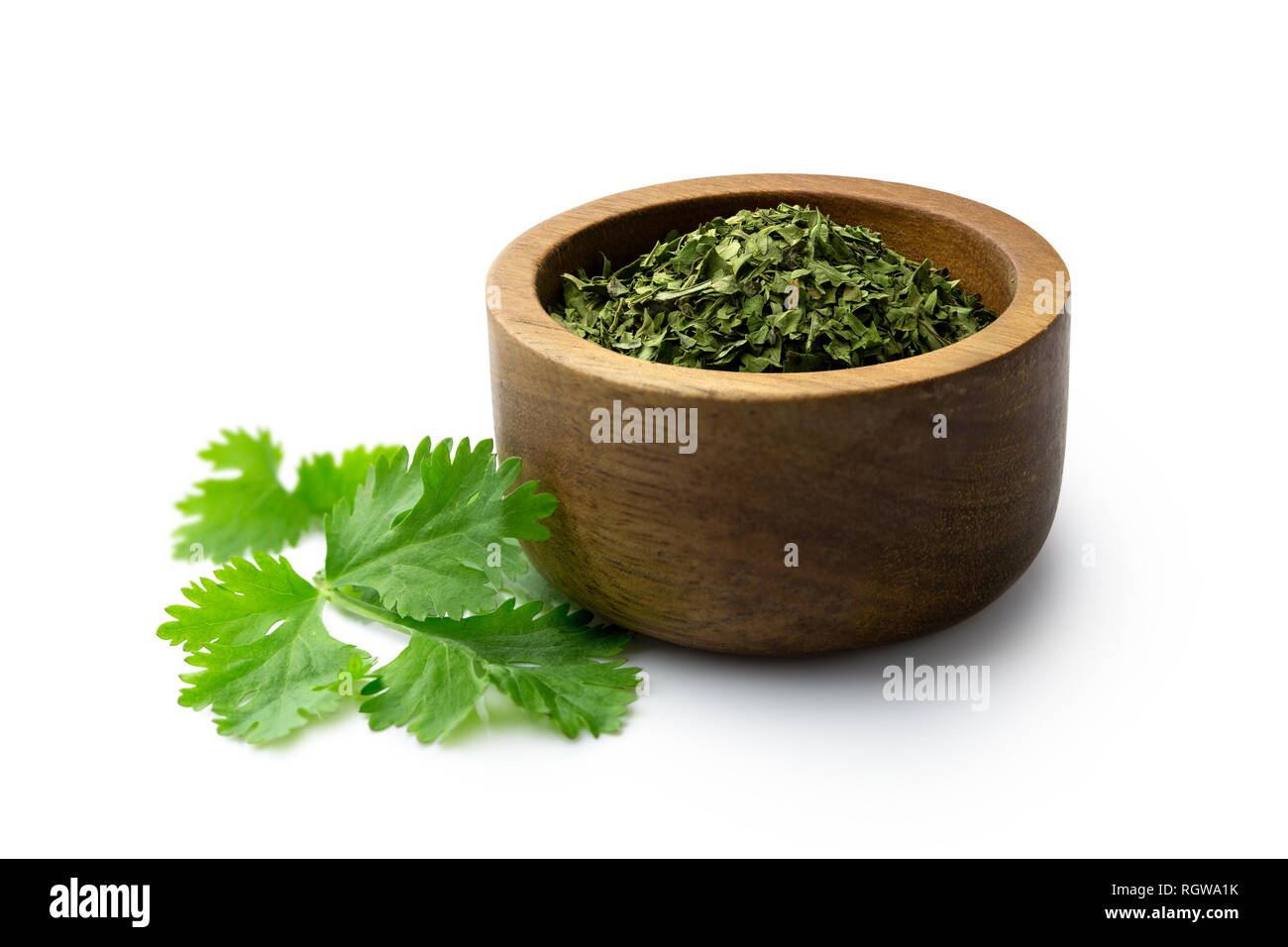 Dried chopped coriander leaves in a dark wood bowl next to fresh ...