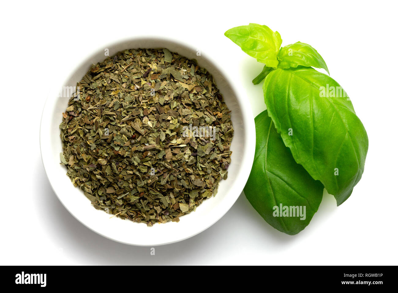 Dried chopped basil in white ceramic bowl next to fresh basil leaves ...