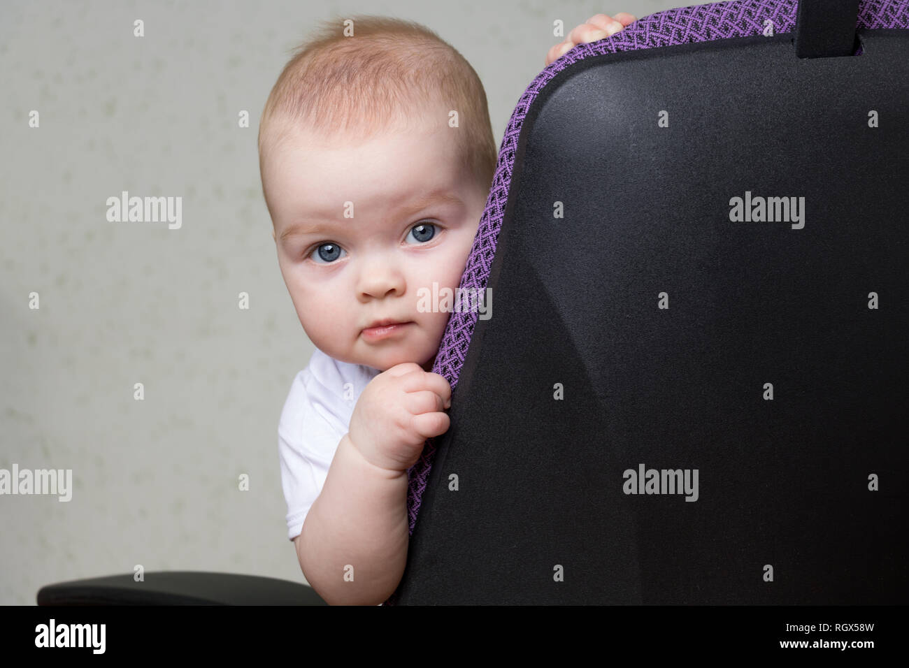 a small child looks out from behind the back of the office chair and ...