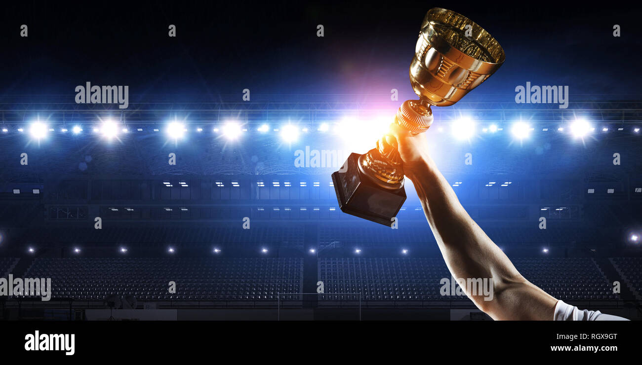 Hand of athlete holding cup trophy against stadium. Mixed media Stock ...