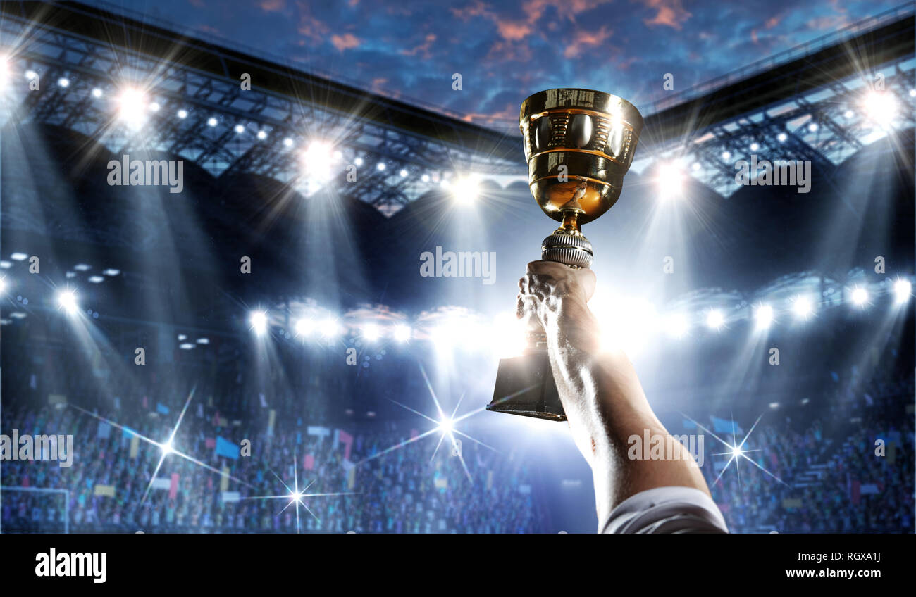 Hand of athlete holding cup trophy against stadium. Mixed media Stock ...