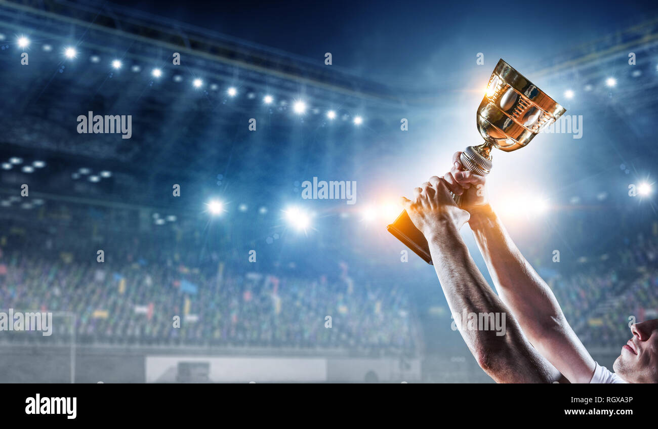 Hand of athlete holding cup trophy against stadium. Mixed media Stock ...